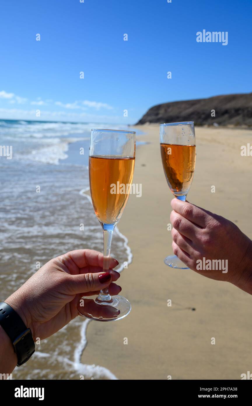 Beach party, hands with glass of rose champagne or cava sparkling wine ...