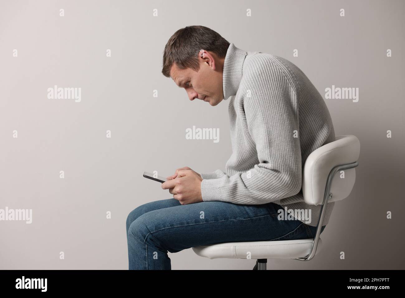 Man with bad posture using tablet while sitting on chair against grey ...