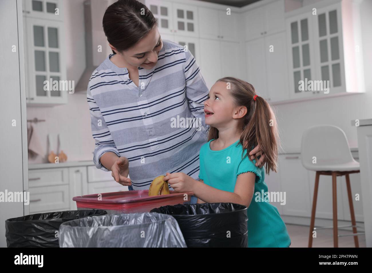 Young woman and her daughter throwing banana peel into trash bin in ...