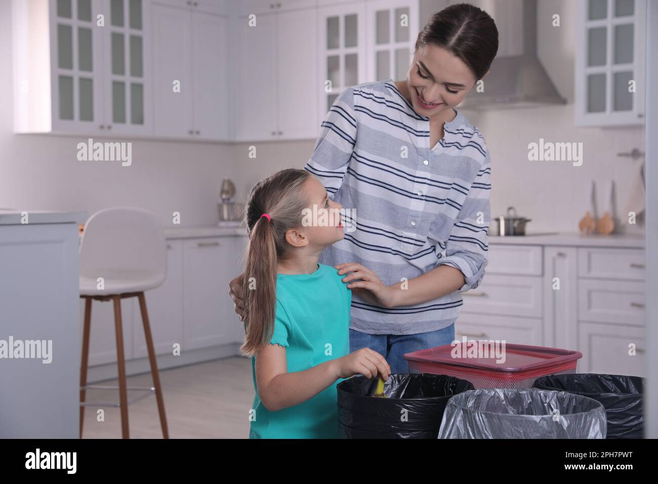Young woman and her daughter throwing banana peel into trash bin in ...
