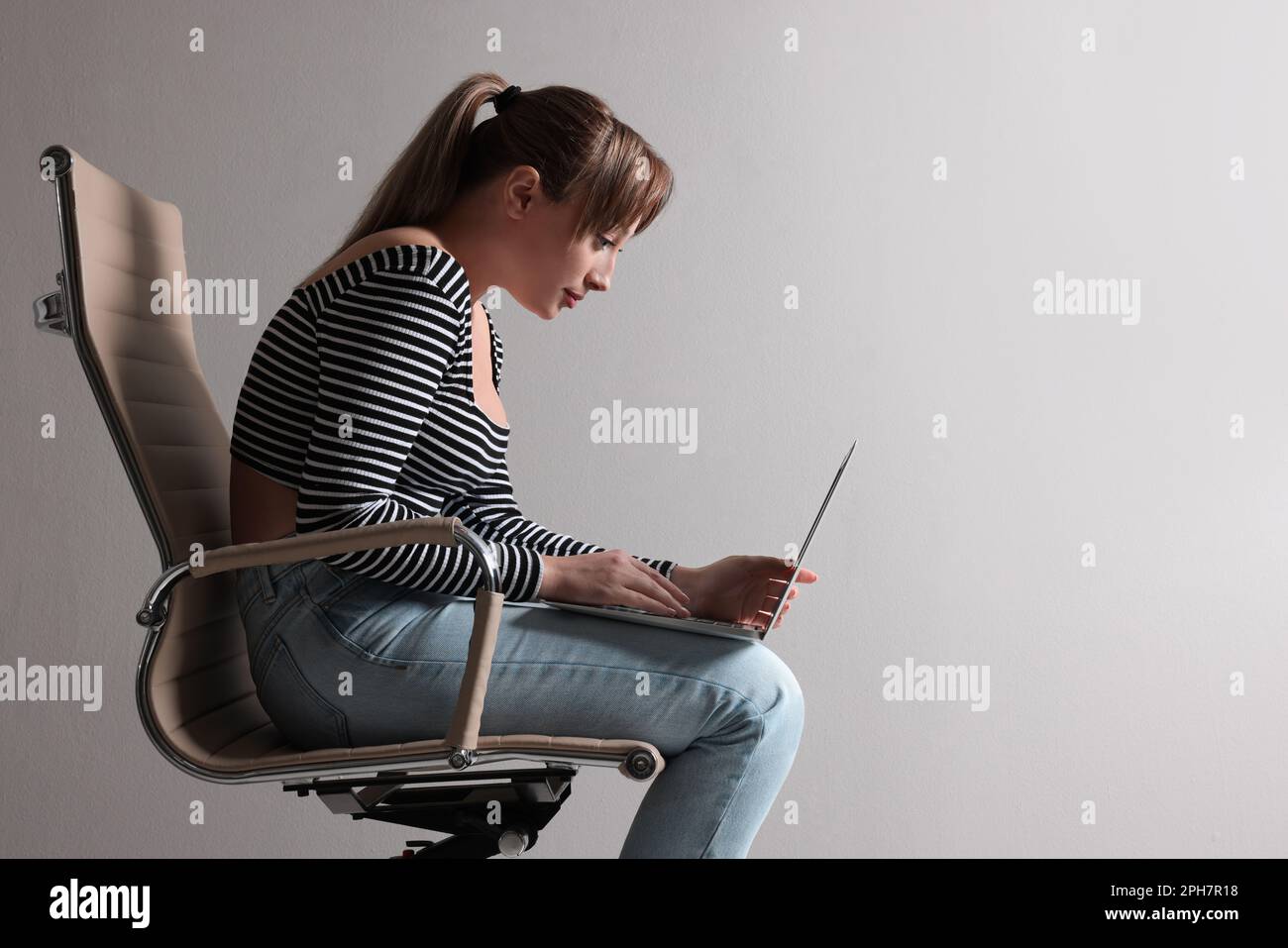 Young woman with poor posture using laptop while sitting on chair ...