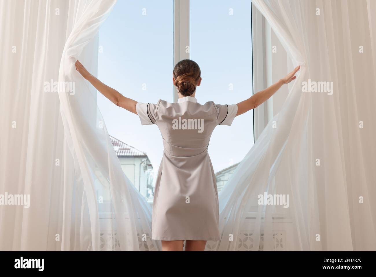 Chambermaid opening window curtains in hotel room, back view Stock ...