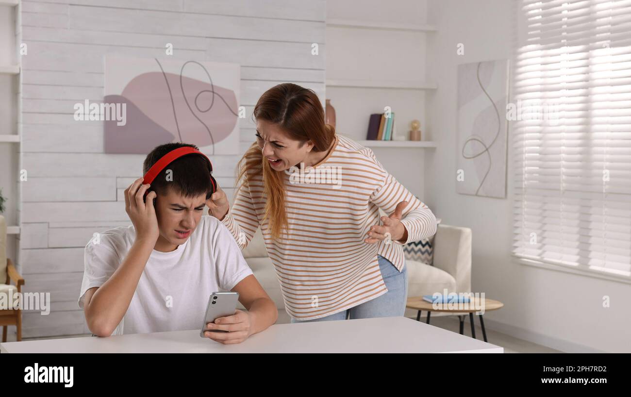 Mother scolding her son while he listening music in headphones at home ...