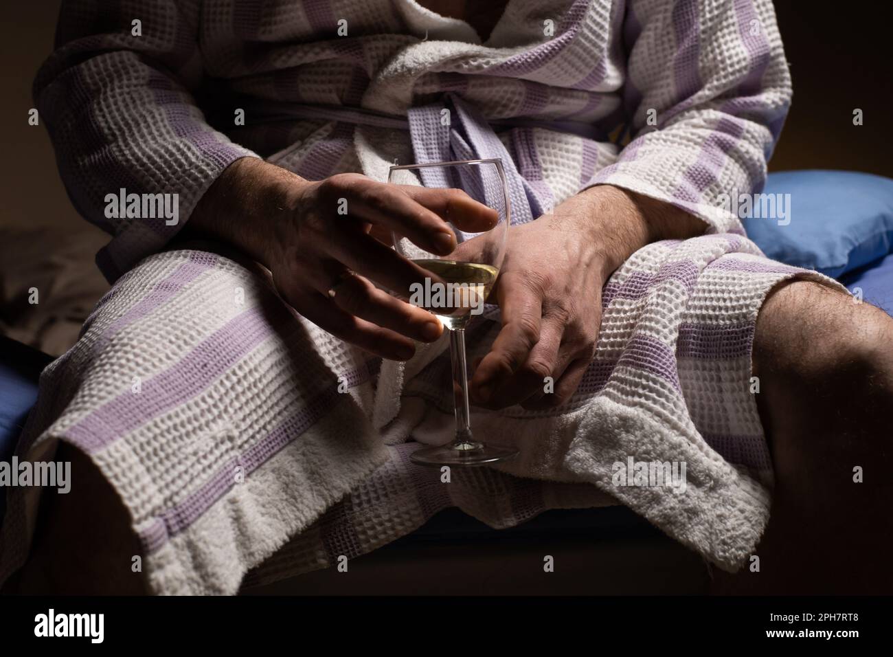 Man and alcoholism. An unrecognizable man in a bathrobe holds a glass ...