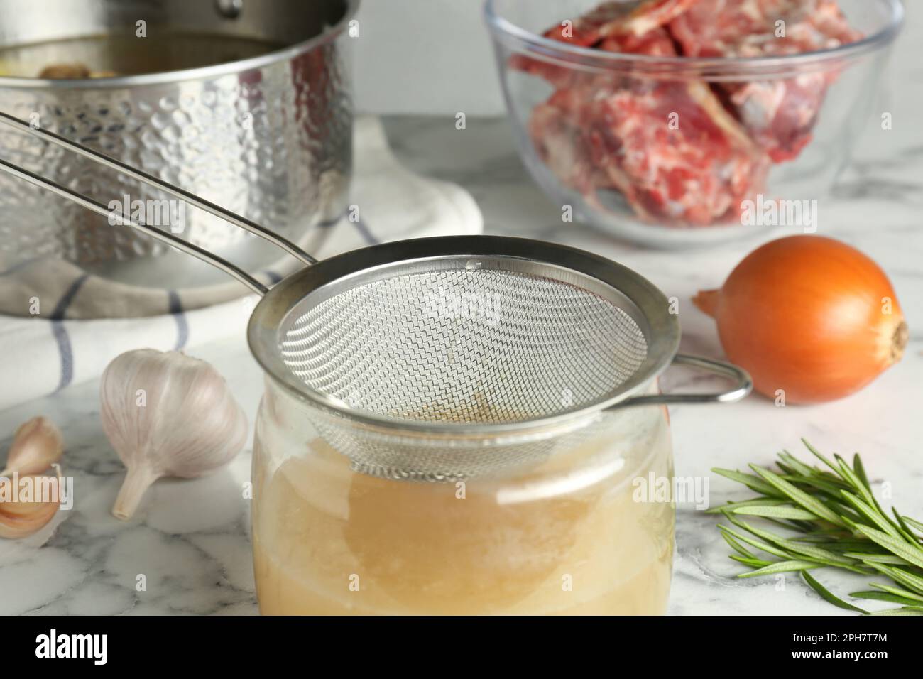 Straining delicious broth through sieve on white marble table, closeup ...