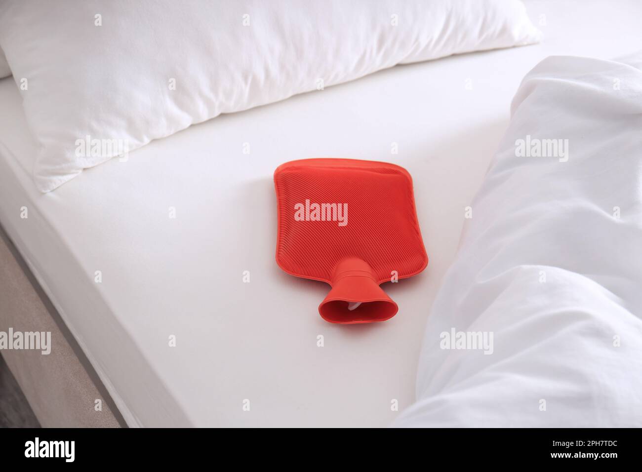 Red hot water bottle on white bed Stock Photo - Alamy