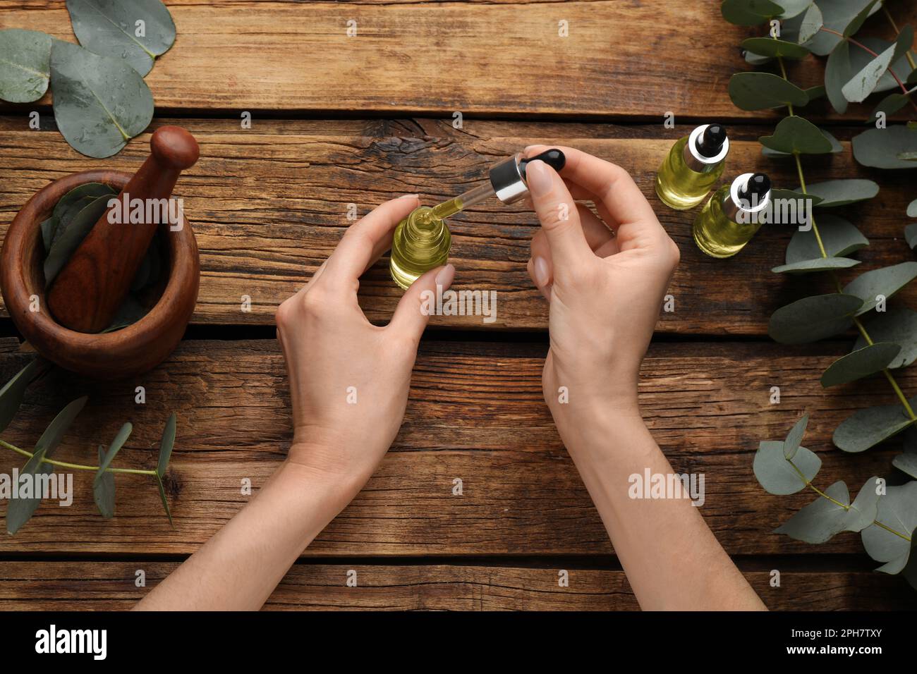 Woman holding bottle of eucalyptus essential oil at wooden table, top ...