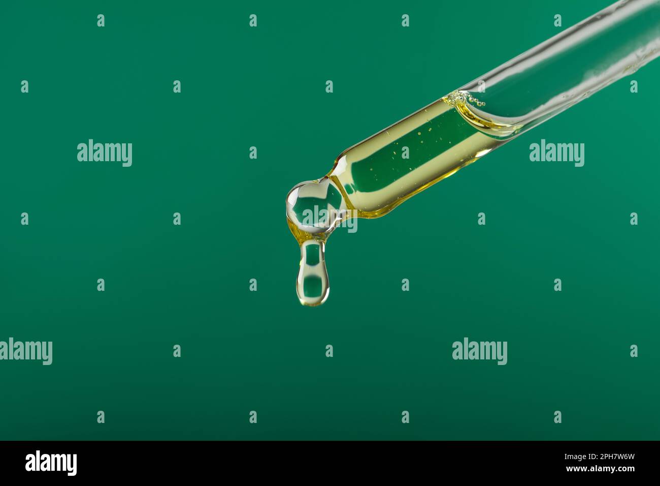 Dripping hydrophilic oil from pipette on green background, closeup ...