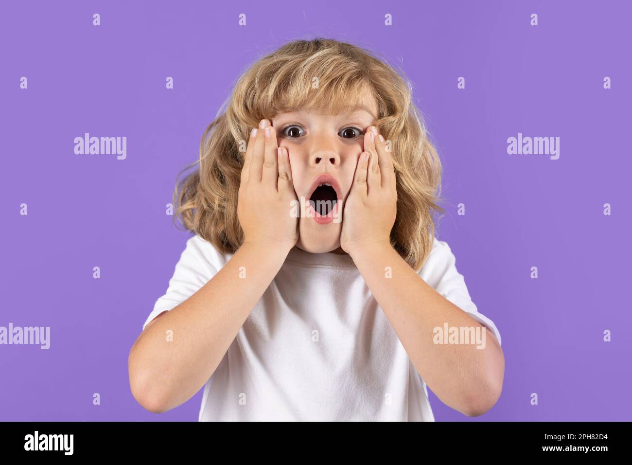 Shocked kid boy keeping hands near cheek with open mouth on studio ...