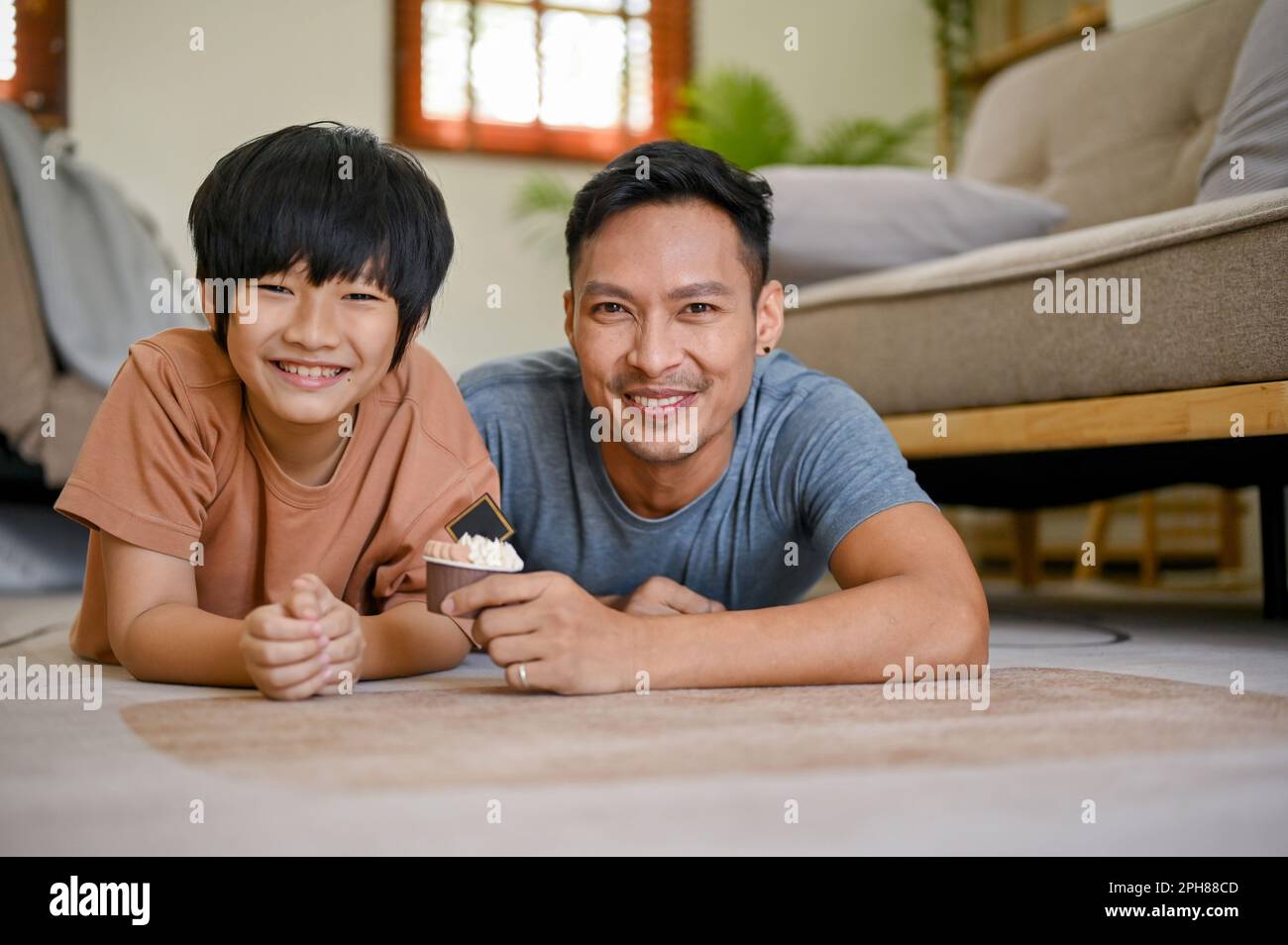 Happy and smiling Asian dad and son laying on the living room floor ...