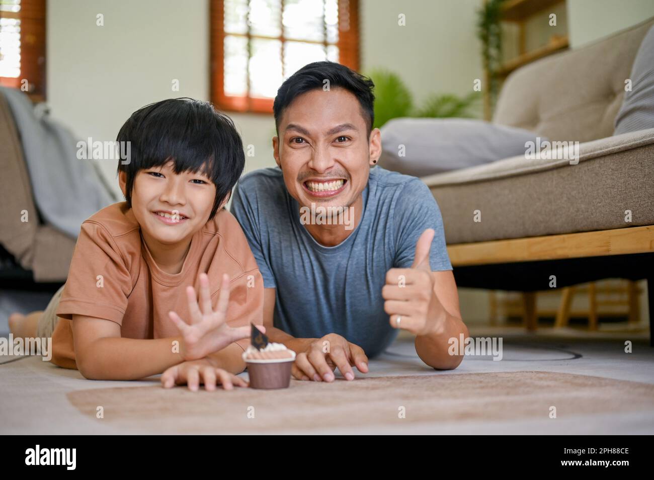 Happy and smiling Asian dad showing thumb up while laying on the living ...