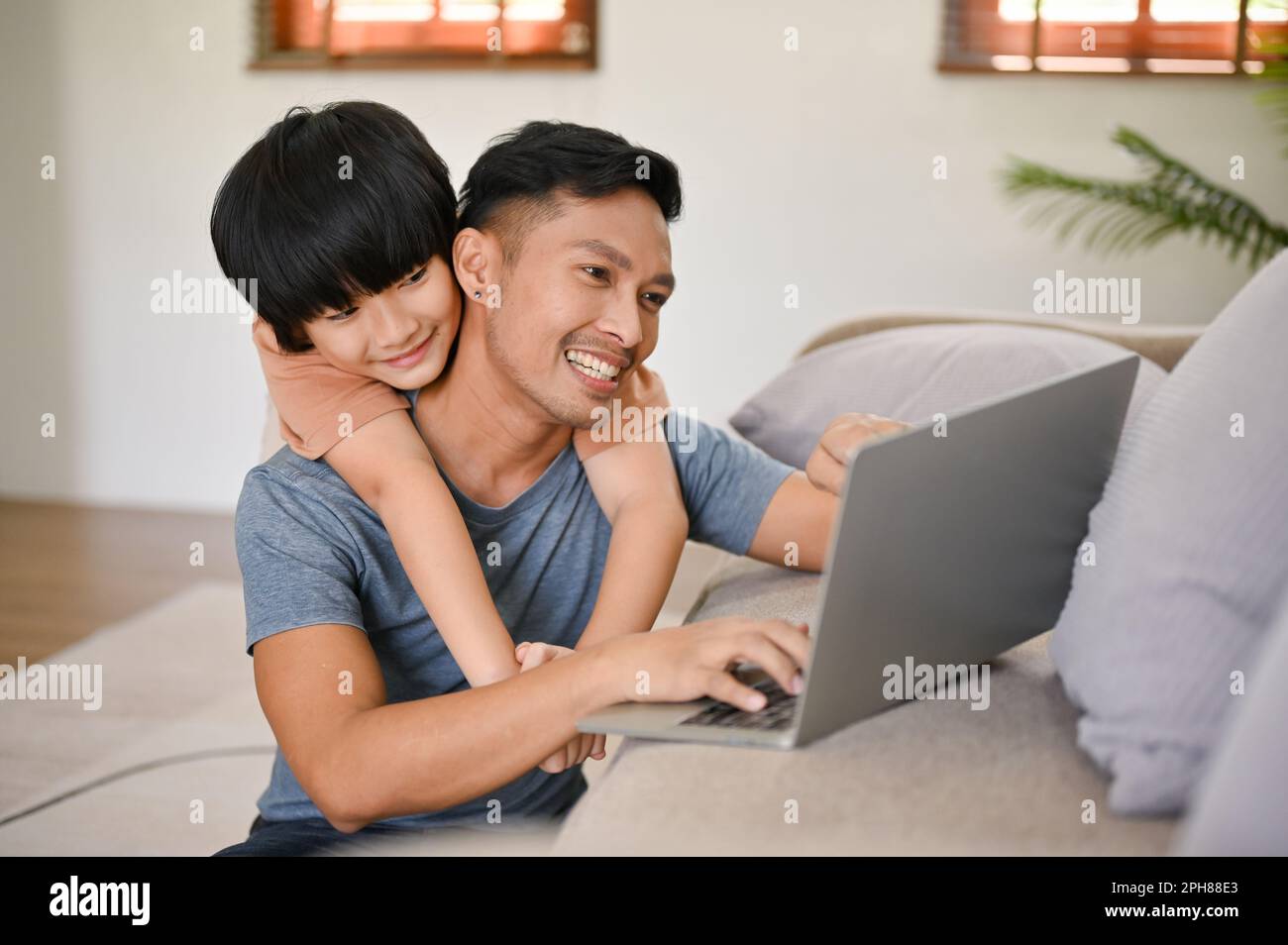 Cute little Asian boy hugging his father from behind while he works on ...