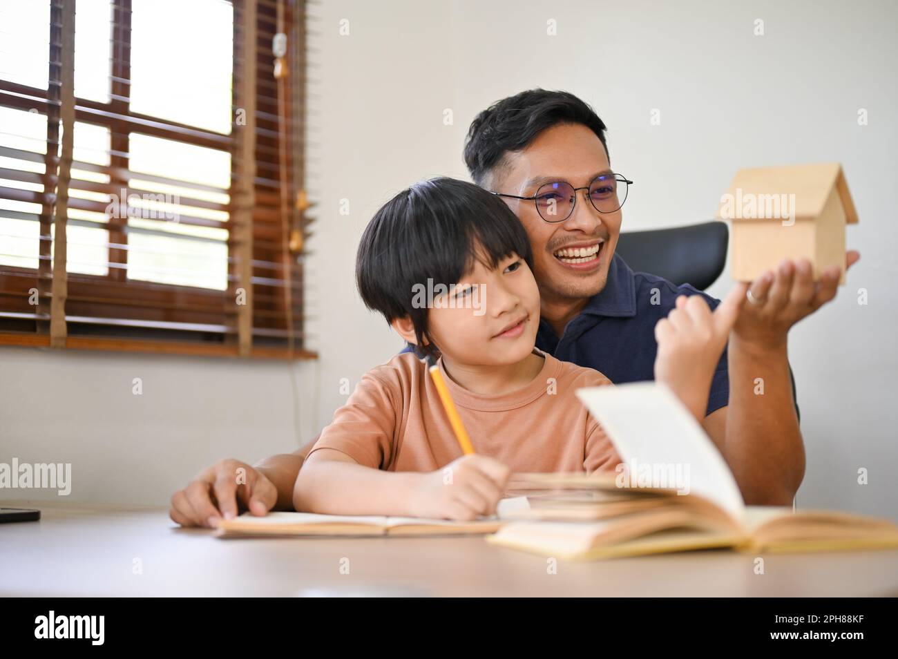 Kind and cheerful Asian dad is teaching his little son to do homework ...