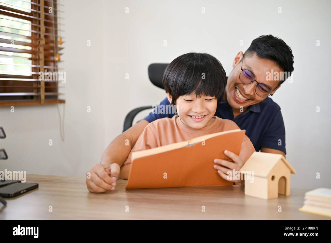 A caring and happy Asian father teaching his son to read a kid's book ...