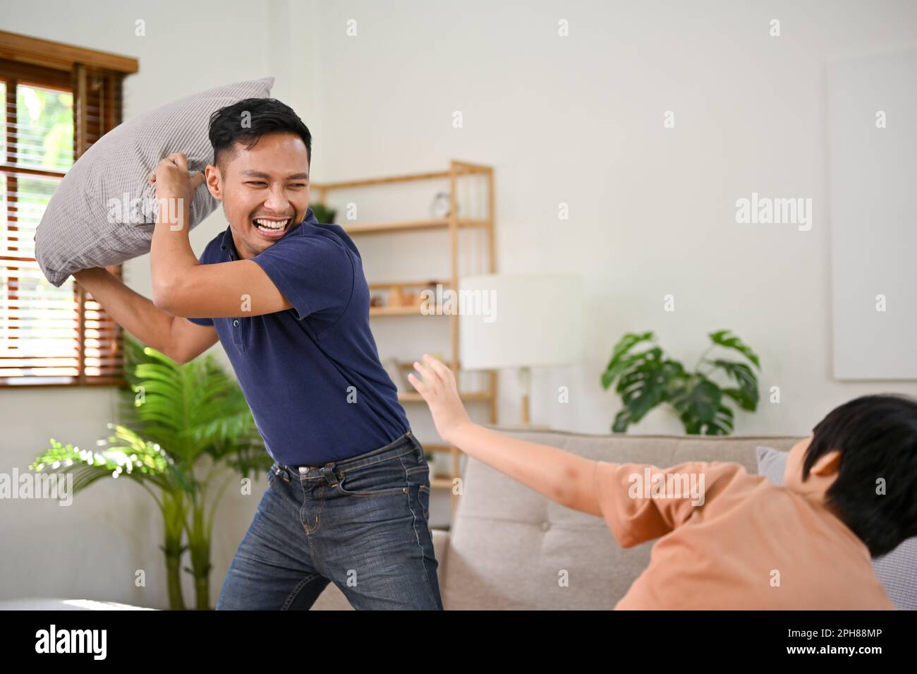 Playful and happy Asian dad enjoying playing pillow fight with his ...