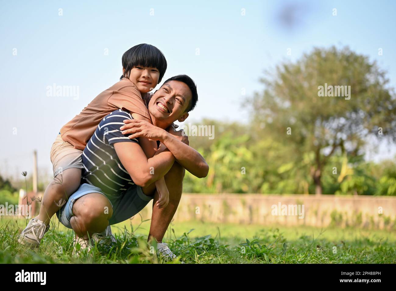 Smiling and happy Asian dad playing with his son in the backyard while ...