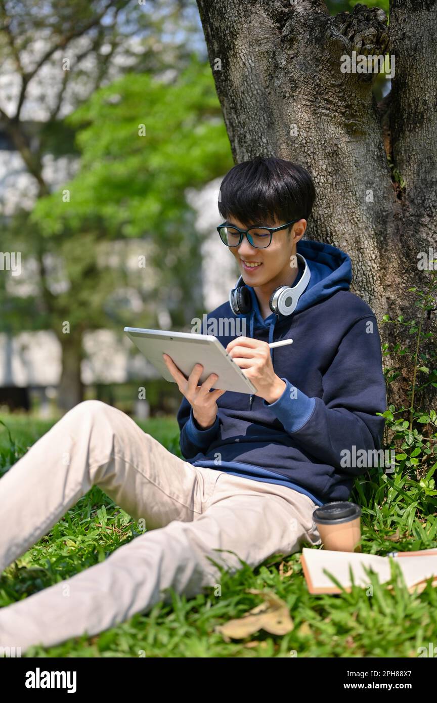 Portrait of a happy young Asian male college student using his digital ...