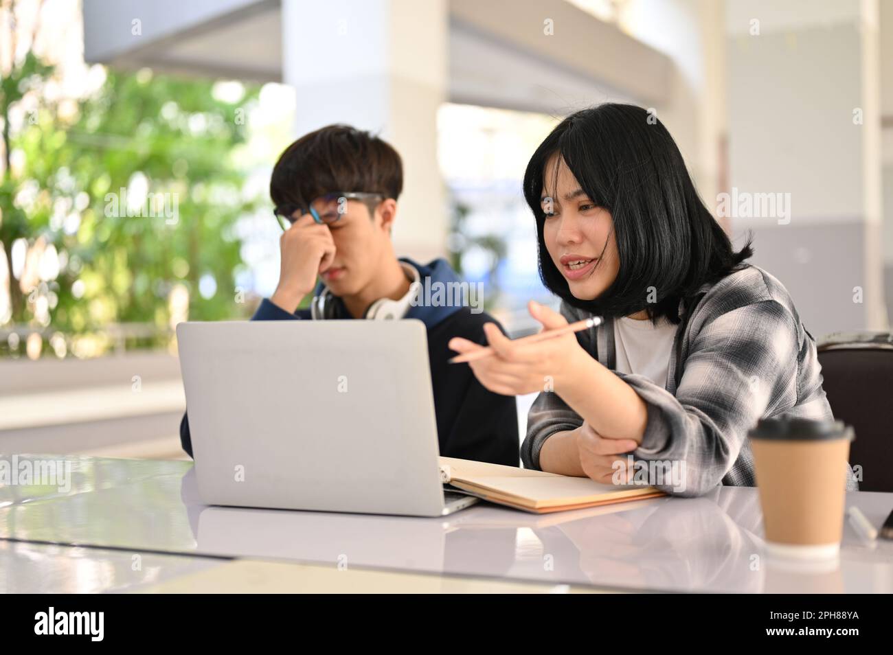 Smart young Asian female college student is tutoring math to her male ...