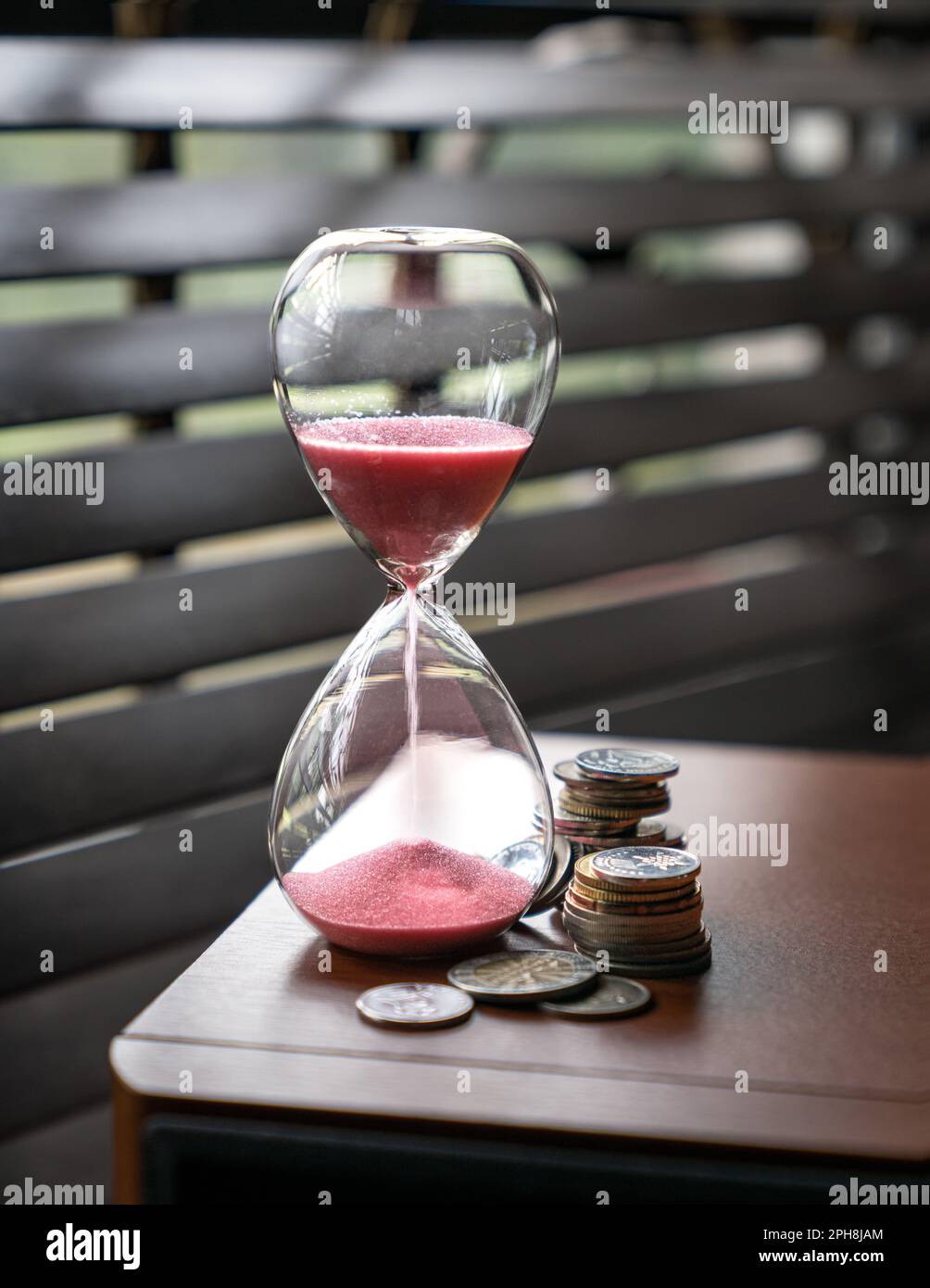 Sand running or flowing down of an hourglass with coins next to it ...
