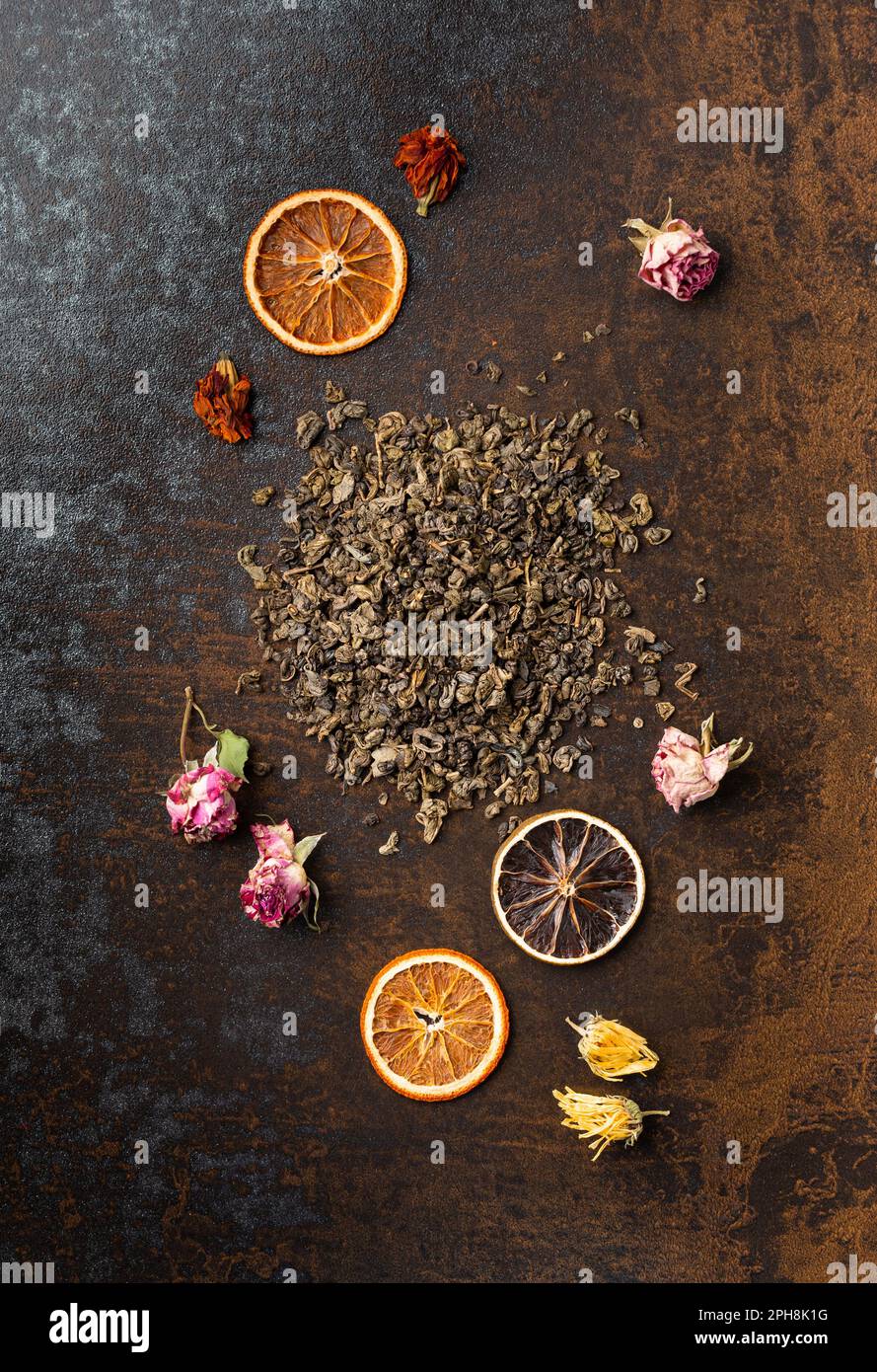 Green dry tea, flower tea and dry orange chips on brown background top ...