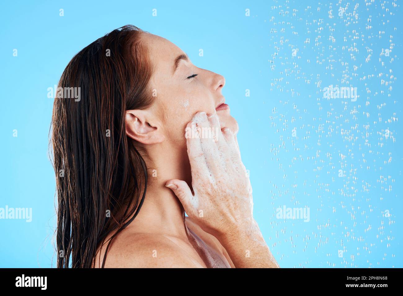 Shower, water and woman soap on face in studio, blue background and ...