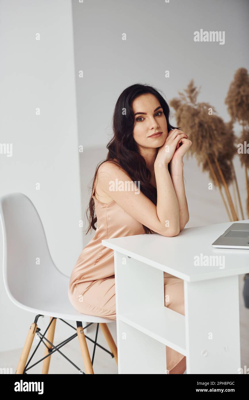 Beautiful brunette with curly hair in luxury clothes sits by table with ...