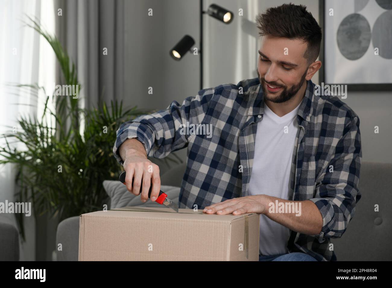 Man using utility knife to open parcel at home Stock Photo - Alamy