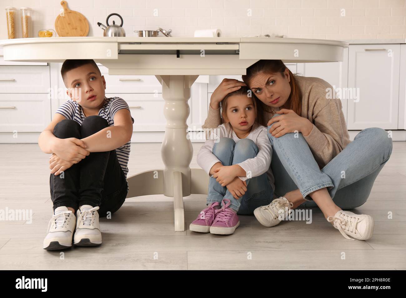 Scared mother with her children hiding under table in kitchen during ...