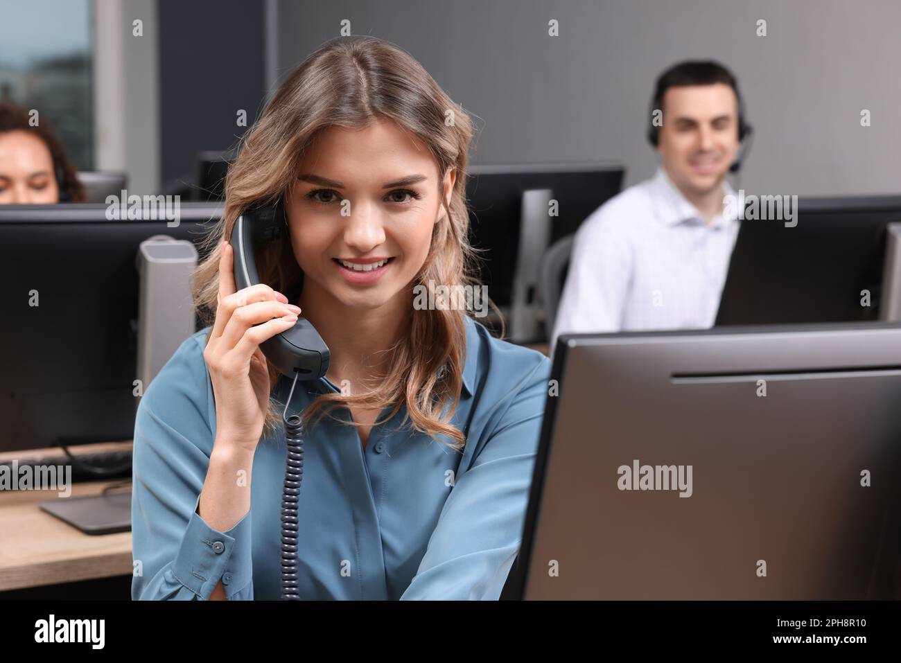 Young call center operator talking on phone and her colleagues working in modern office Stock ...