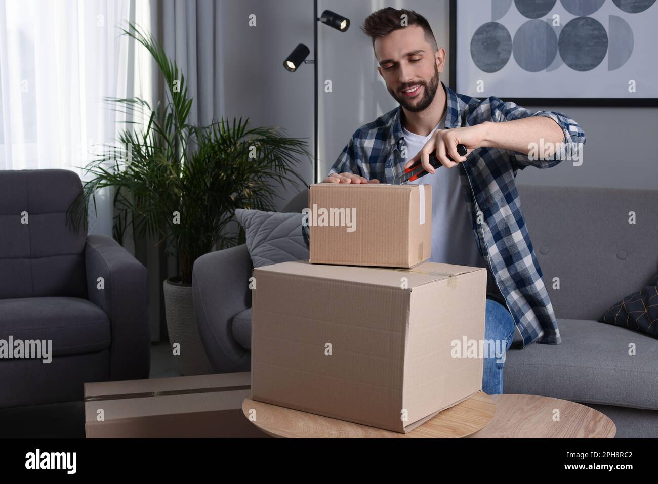 Man using utility knife to open parcel at home Stock Photo - Alamy