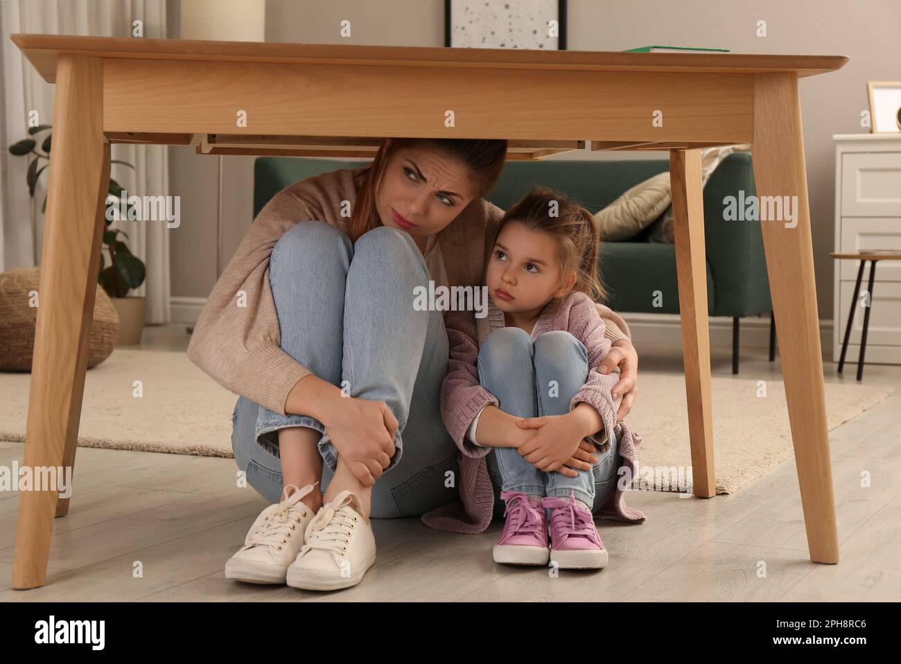 Scared mother with her little daughter hiding under table in living ...