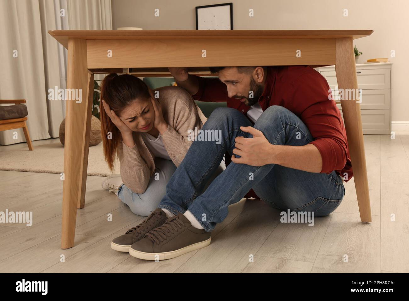 Scared couple hiding under table in living room during earthquake Stock ...