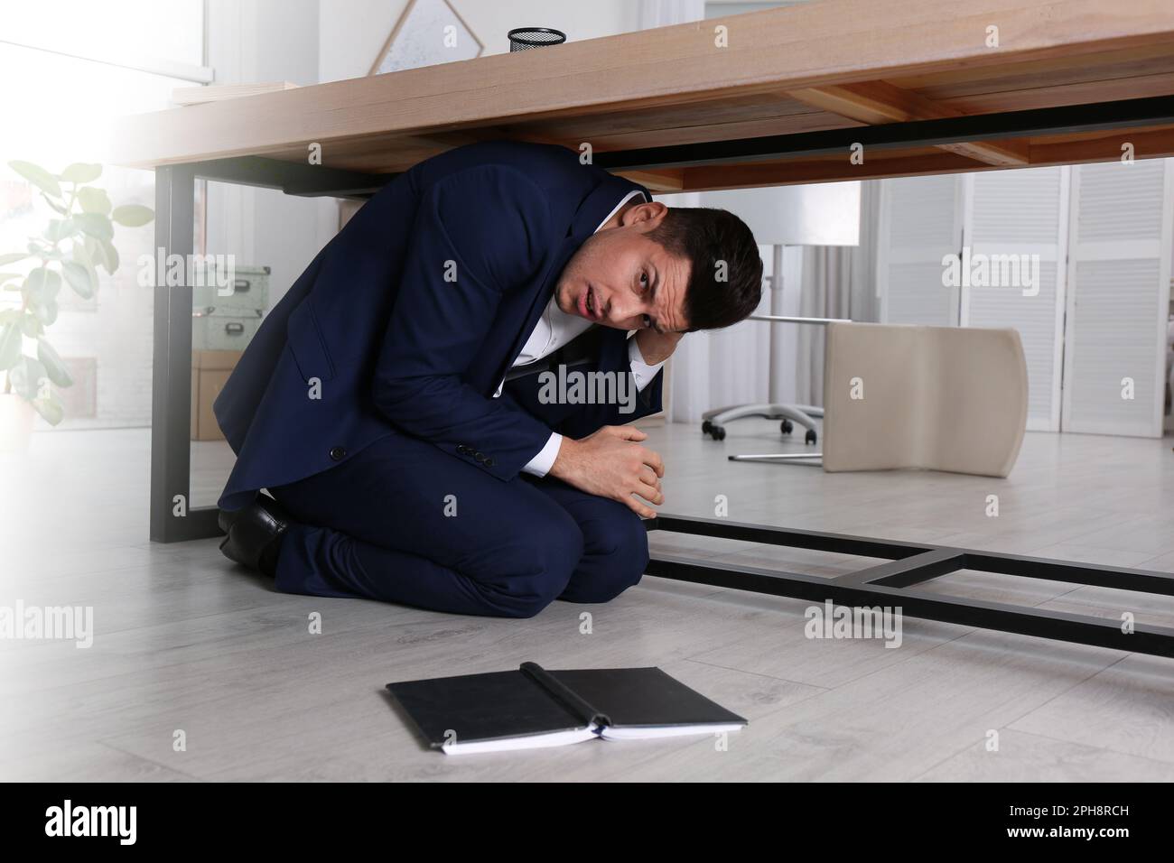 Scared man hiding under office desk during earthquake Stock Photo - Alamy