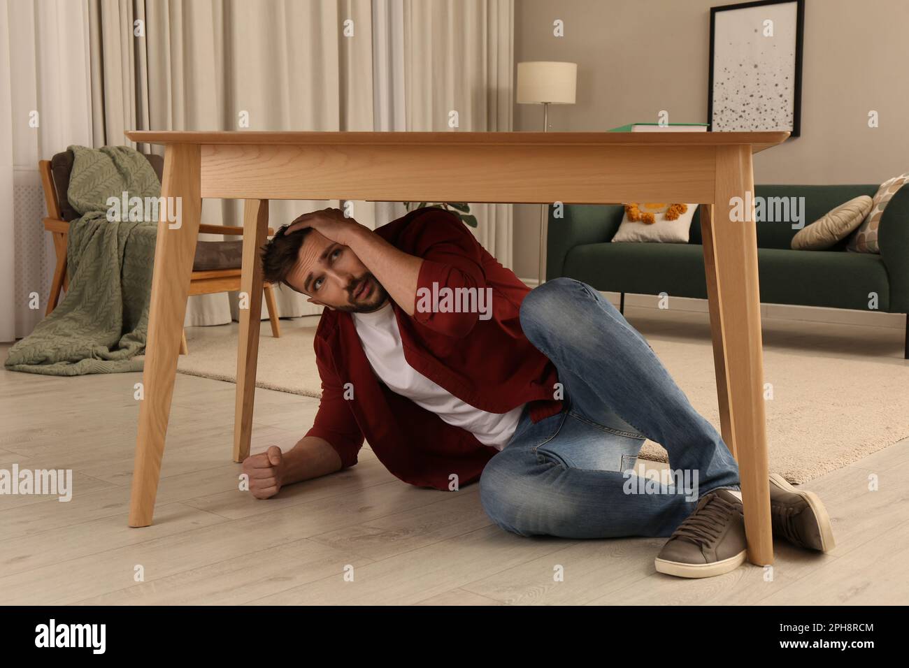 Scared man hiding under table in living room during earthquake Stock ...