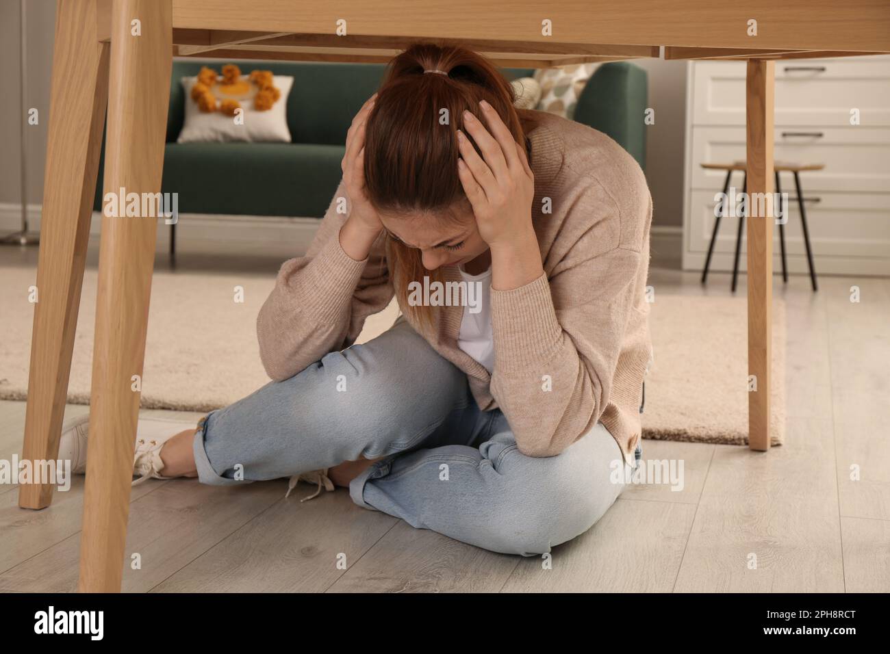 Scared woman hiding under table in living room during earthquake Stock ...