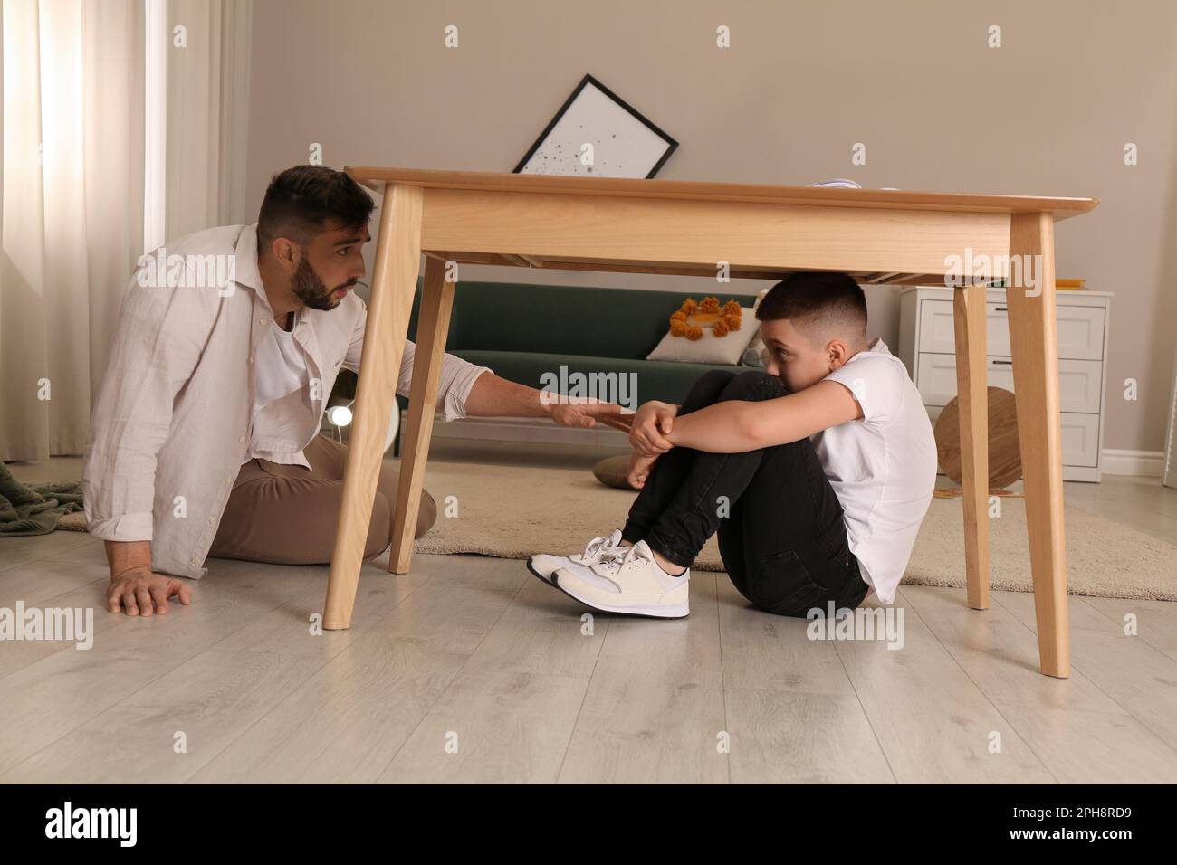 Father comforting his scared son under table in living room during ...