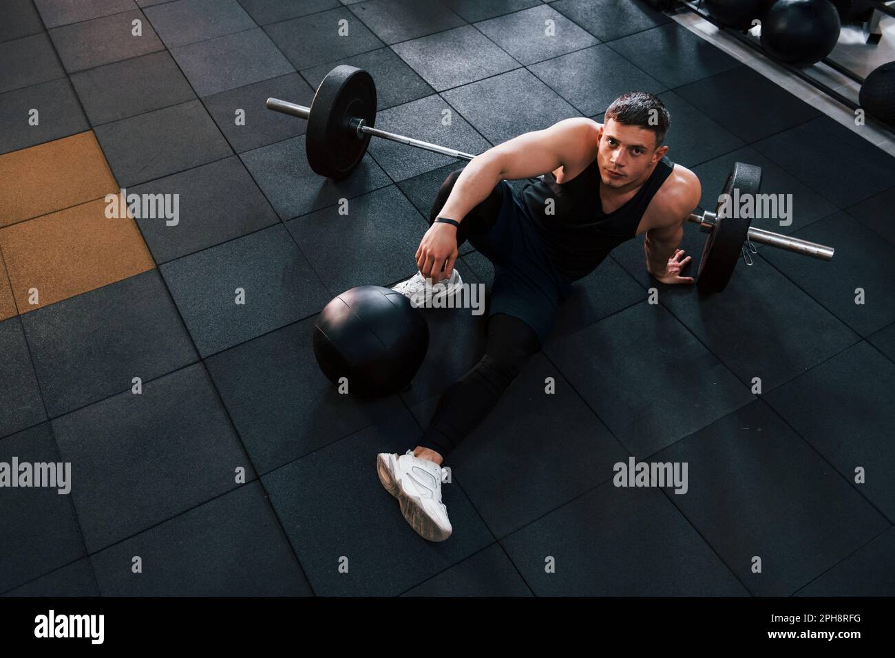 Strong man in sportive clothes sitting on the floor in the gym with ...