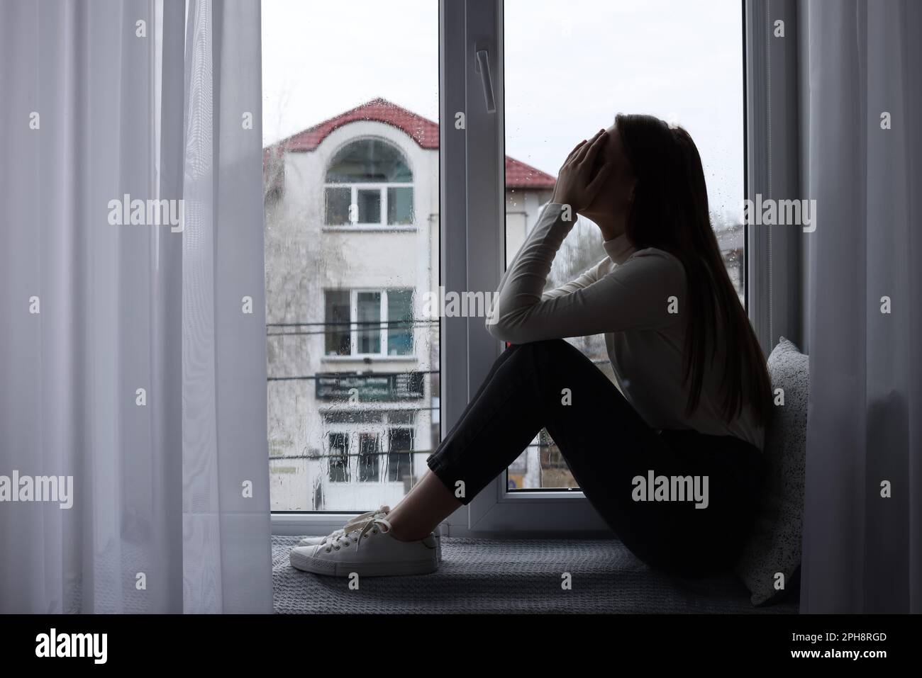 Unhappy young woman crying near window indoors, space for text ...