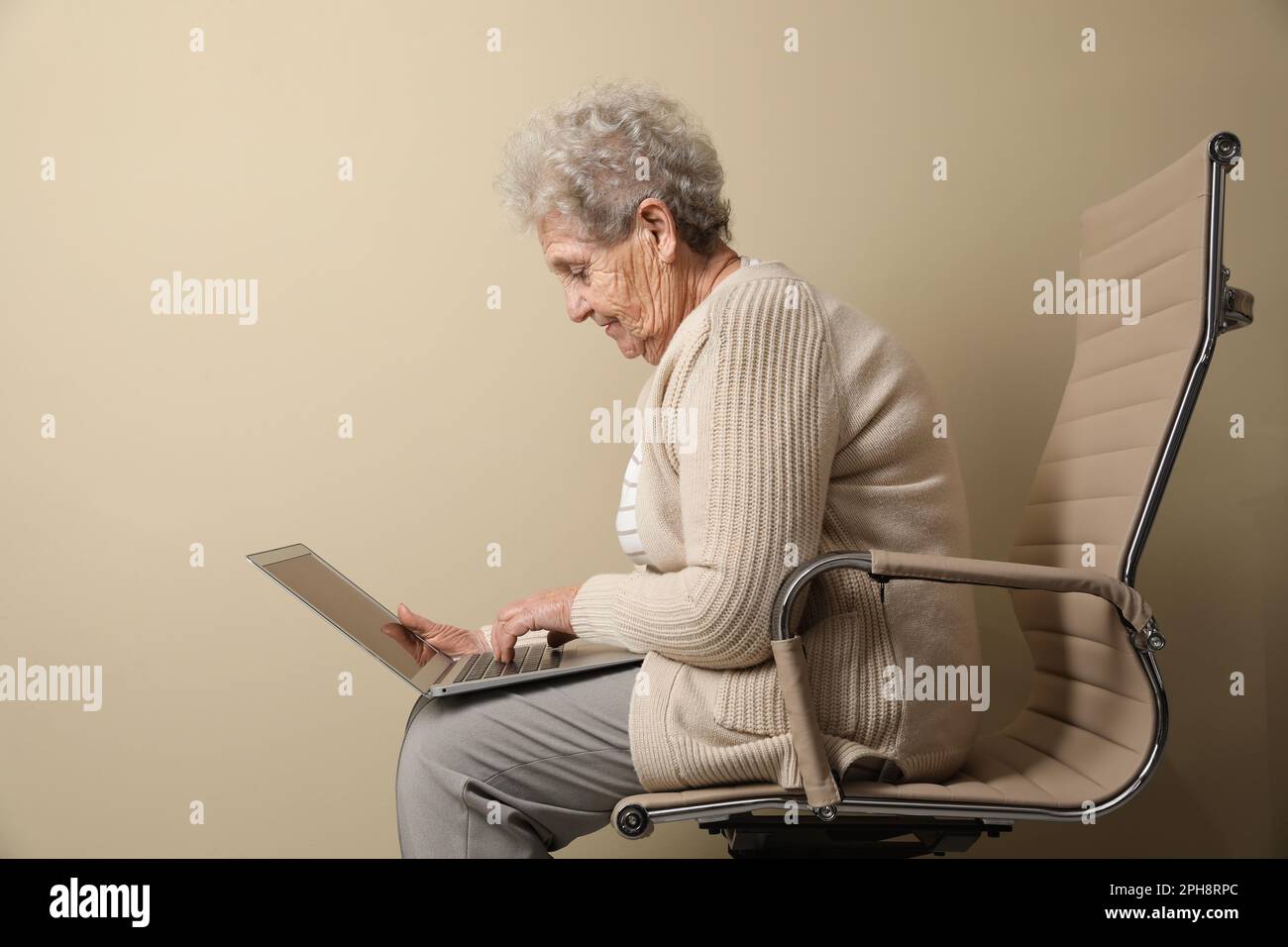 Elderly woman with poor posture using laptop on beige background Stock ...