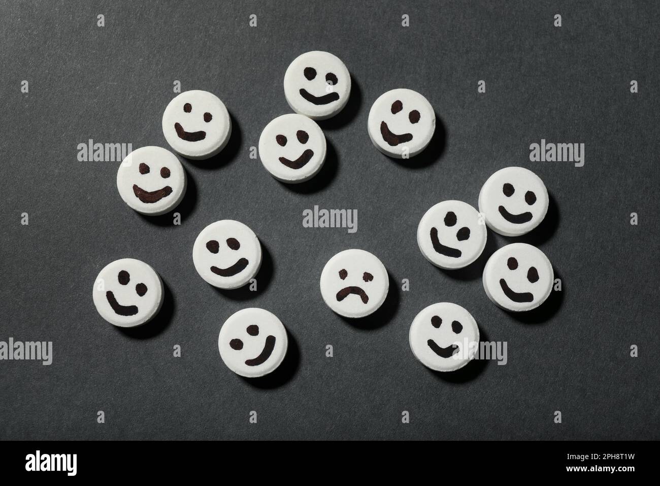 Pill with sad face among happy ones on black background, flat lay ...
