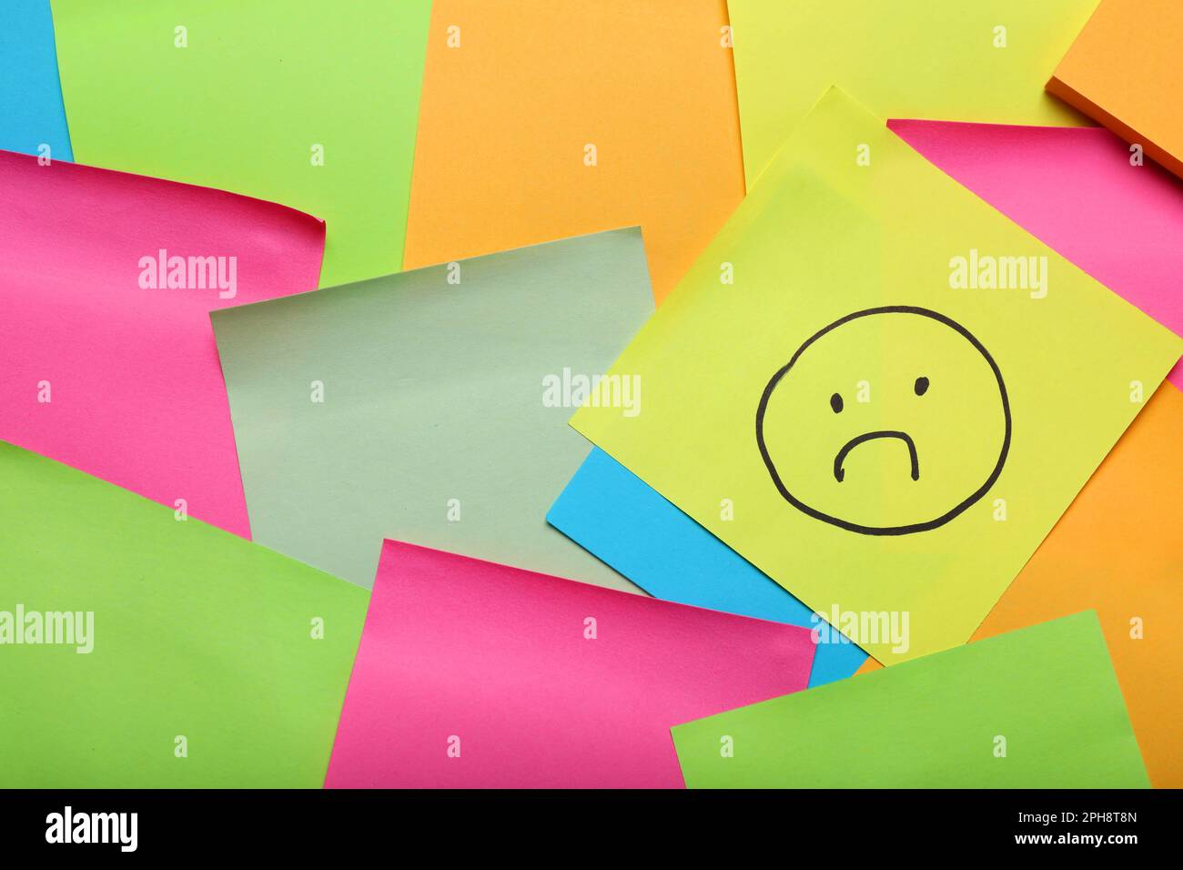 Sticky note with sad face among colorful paper, top view. Space for ...