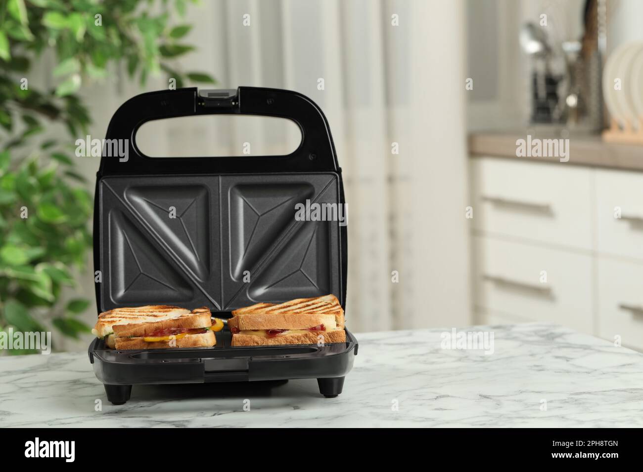 Modern grill maker with sandwiches on white marble table in kitchen ...