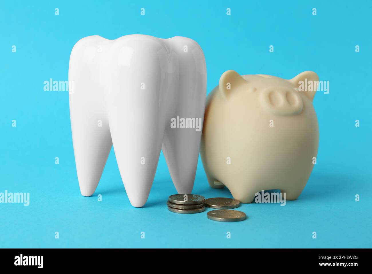 Ceramic model of tooth, piggy bank and coins on light blue background ...