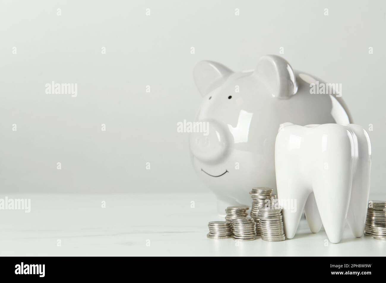 Ceramic model of tooth, piggy bank and coins on white table, space for ...