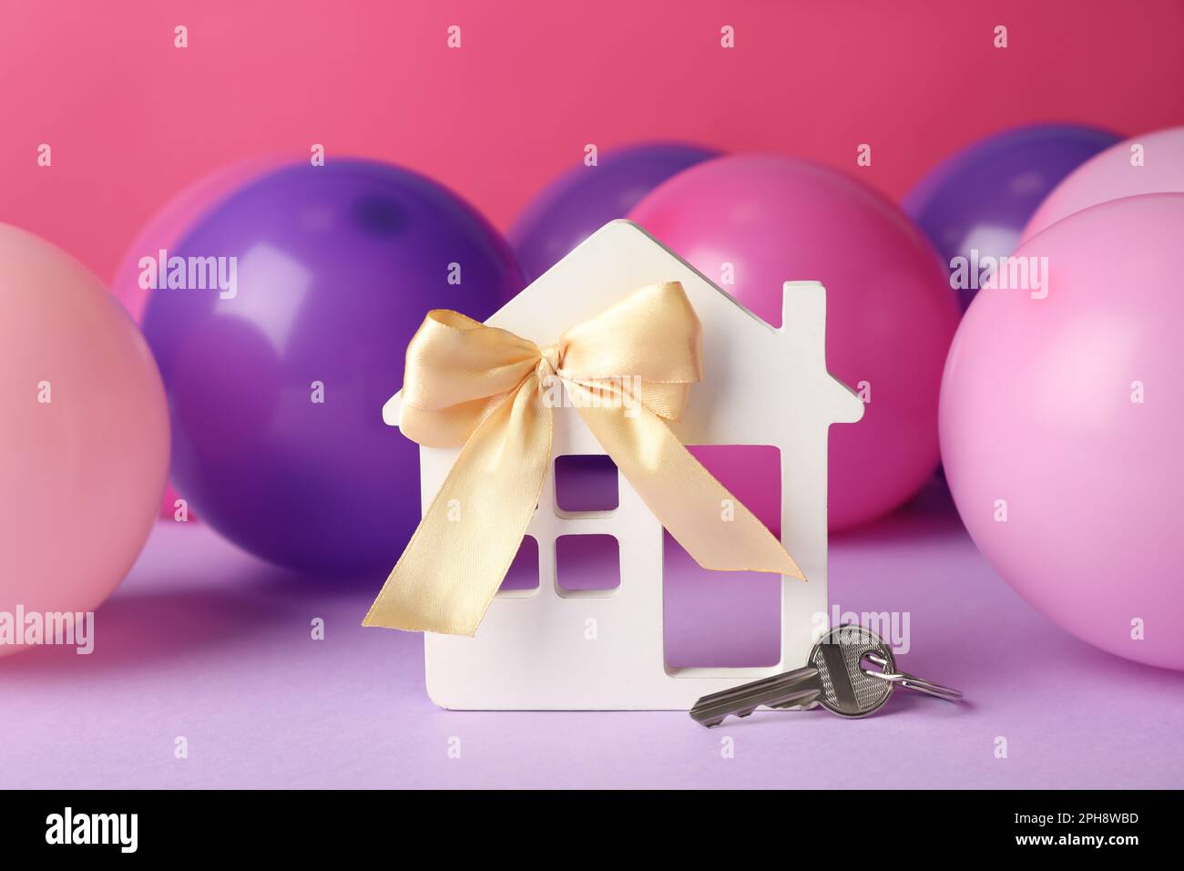 House model with bow, key and colorful balloons on violet table ...