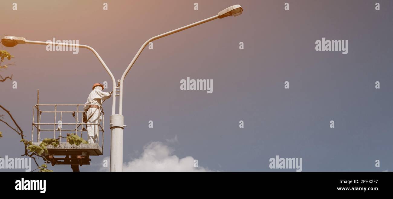 man stands on a tower and paints a lamppost. Men in cradle painting ...