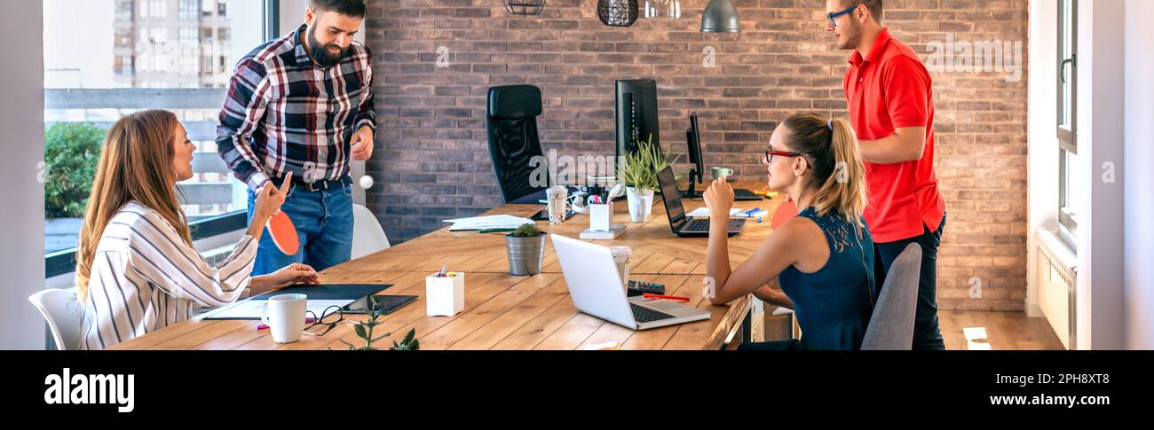 Colleagues talking in office while two of them having fun playing ping ...