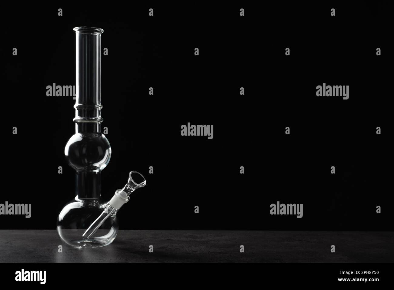 Glass bong on grey table against black background, space for text ...