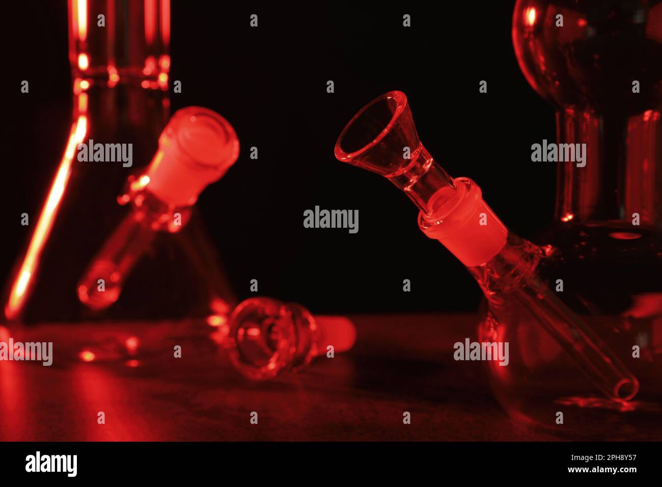 Glass bongs on table against black background, toned in red. Smoking ...