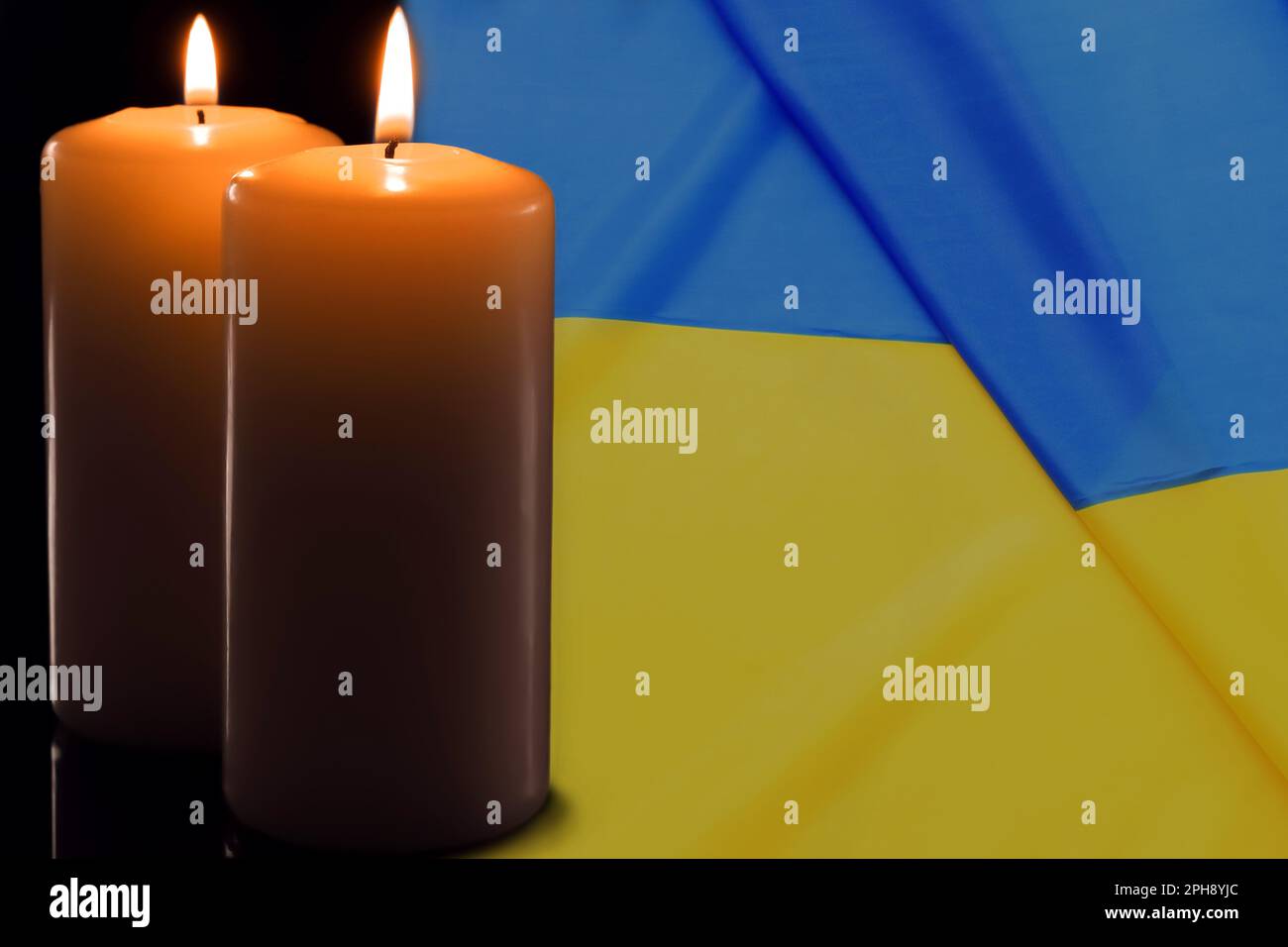 Two burning candles and Ukrainian national flag on black background ...